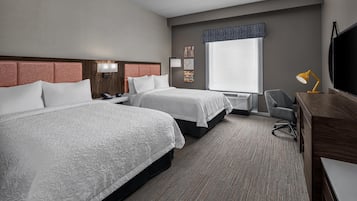Quarto de hotel com duas camas, uma escrivaninha, uma cadeira, uma televisão e obras de arte na parede.