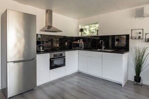 Cozinha moderna com geladeira de aço inoxidável, painel de fundo de mármore preto, armários brancos e janela que ilumina naturalmente o espaço.