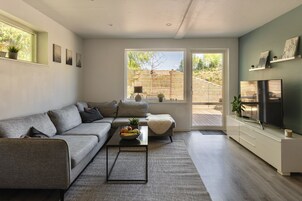 Uma sala de estar moderna com um sofá cinzento, uma mesa de centro com frutas e uma TV sobre um móvel.