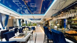 Um restaurante moderno com um balcão comprido, cadeiras de veludo azul e um espaço de bar com copos de vinho.
