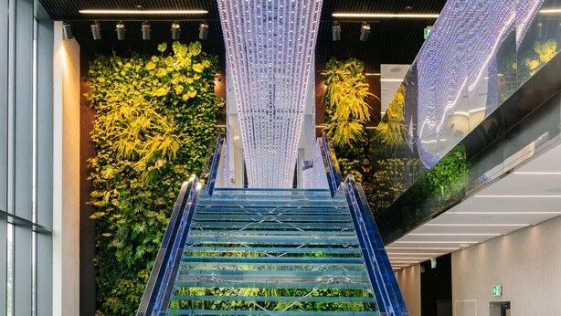 Uma escadaria moderna com degraus de vidro e um lustre decorativo acima.