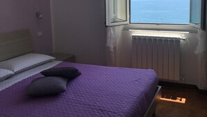 Quarto com cama, janela vista para o mar e radiador.