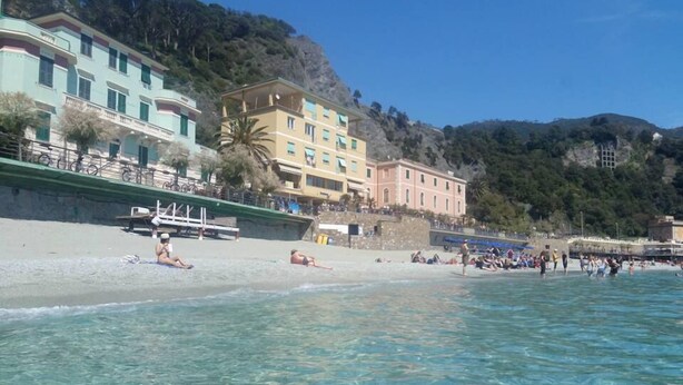 Uma praia com águas cristalinas, pessoas tomando sol e edifícios coloridos ao fundo.