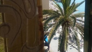 Uma varanda com vista para uma praia, palmeiras e montanhas ao longe.