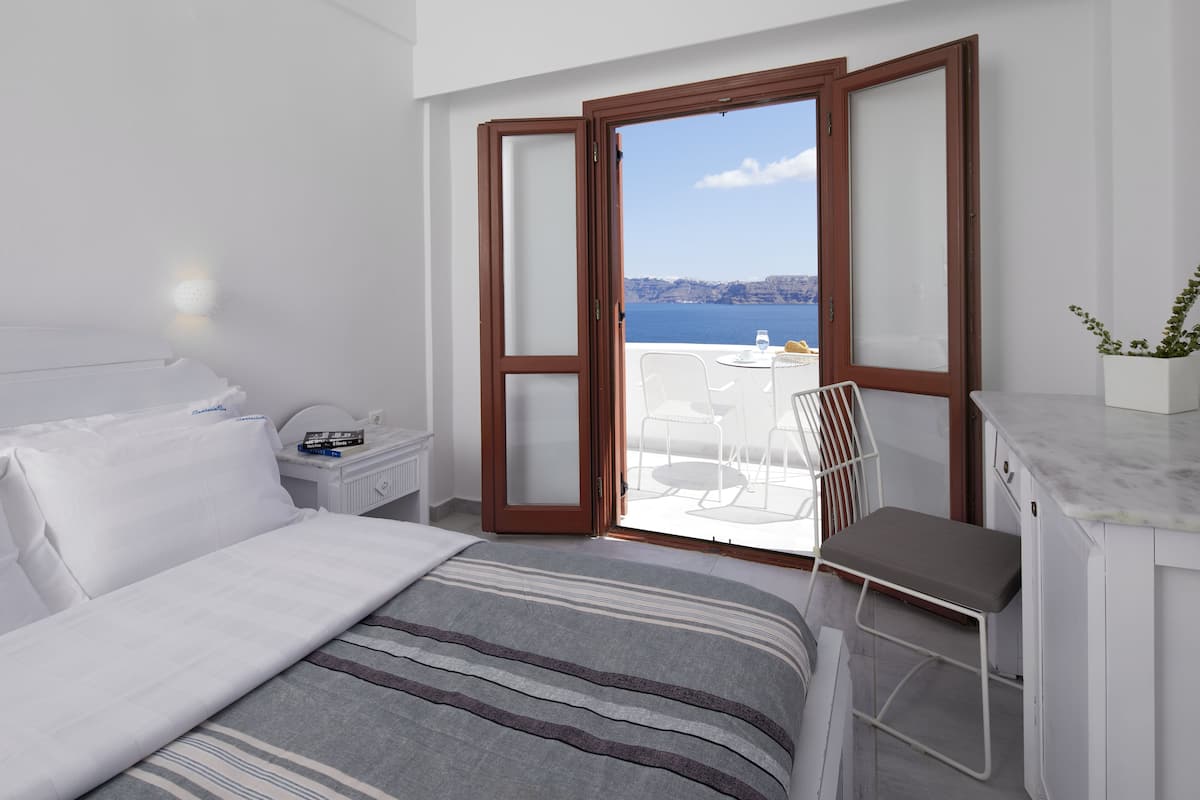 Quarto com cama, escrivaninha, cadeira e vista para o mar.