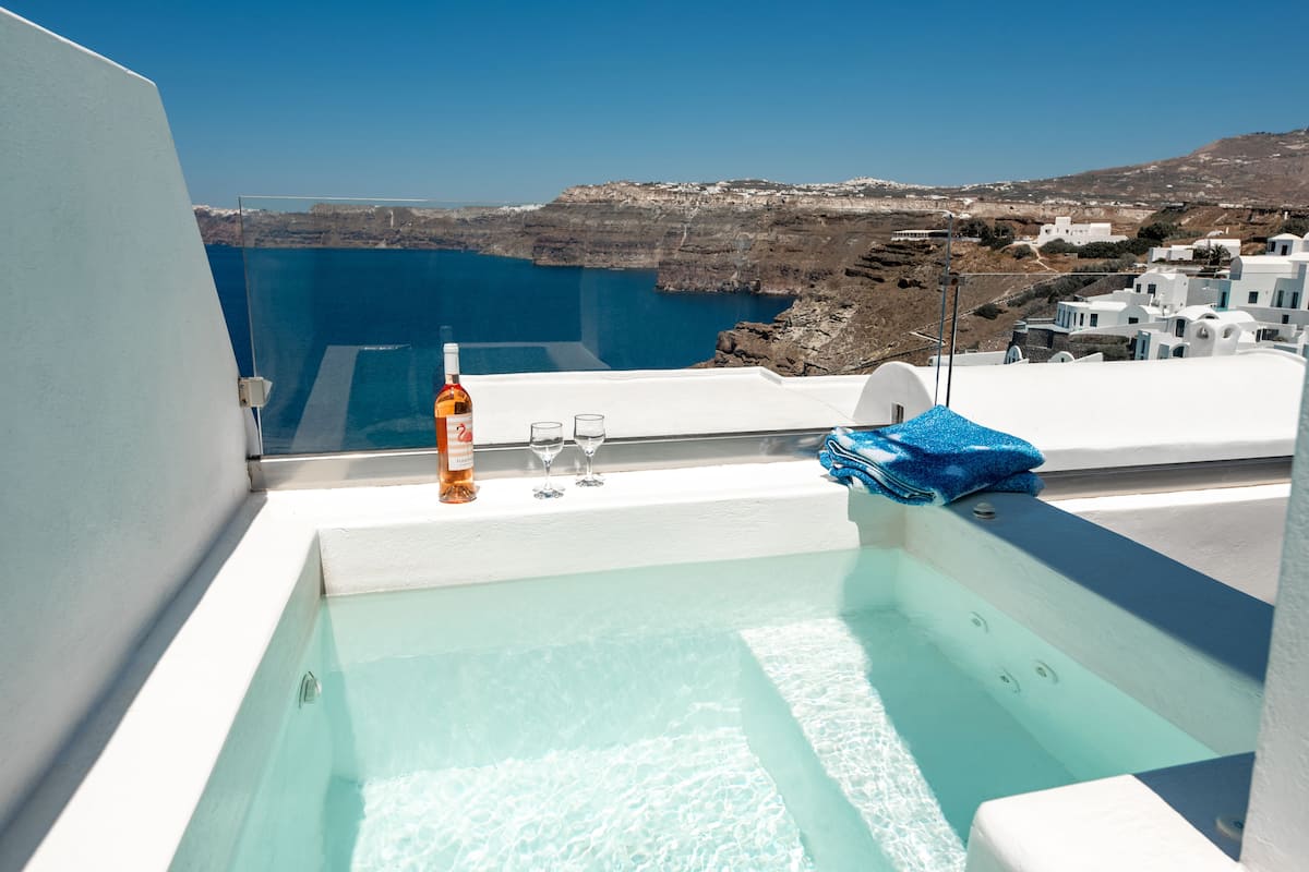 Piscina infinita no terraço com vista deslumbrante para o mar e uma garrafa de vinho.