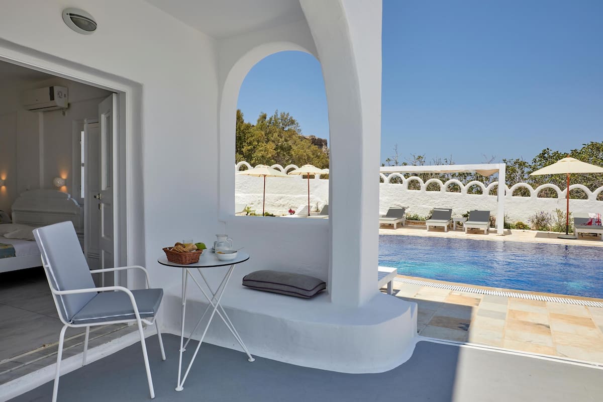 Quarto moderno com vista para piscina, uma cadeira branca, uma mesa pequena com um cesto e um almofada.