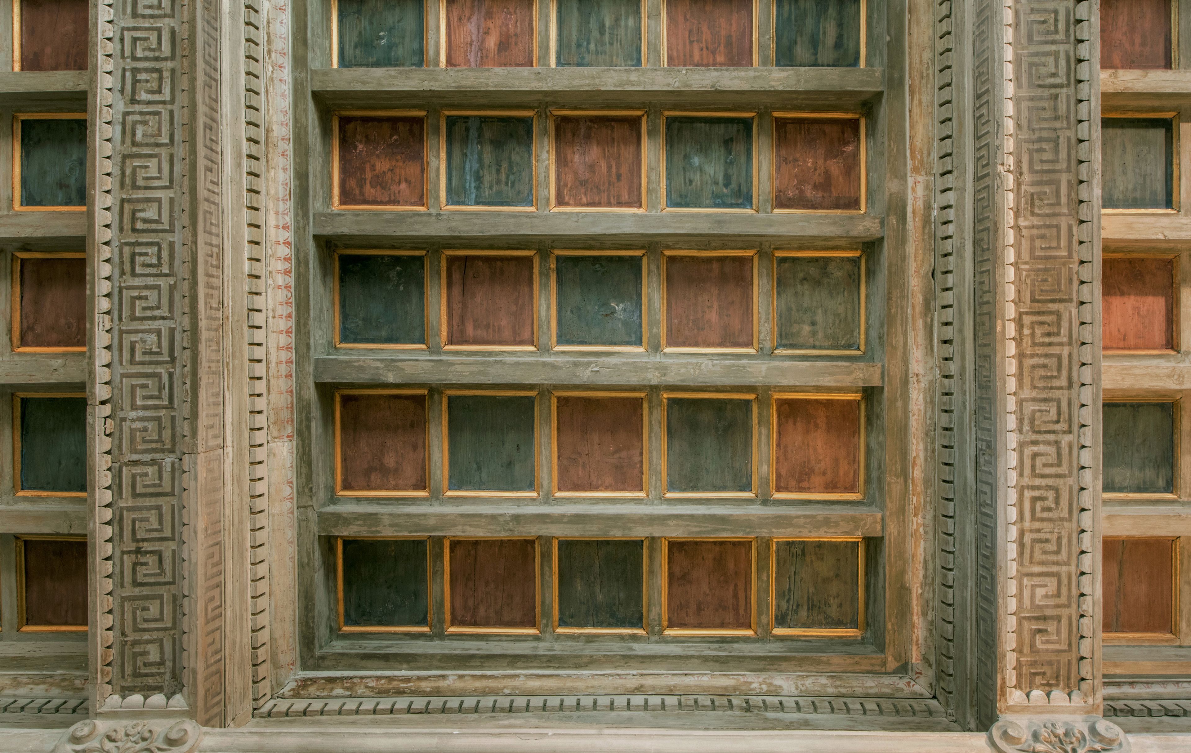 Visão detalhada de uma janela com uma grade de pequenas divisórias, emoldurada por colunas ornamentadas com padrão geométrico.