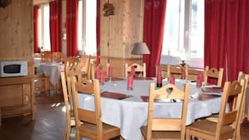 Uma sala de jantar com mesas redondas, cadeiras de madeira e cortinas vermelhas.