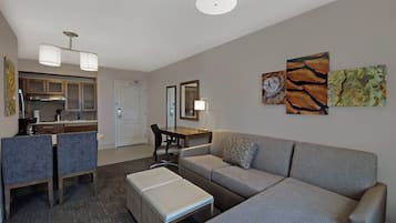 Uma sala de estar moderna com sofá, mesa de centro e área de jantar com mesa e cadeiras. Uma cozinha é visível ao fundo.