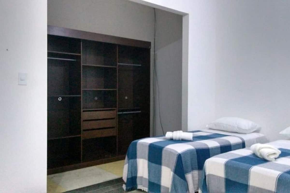 Quarto com duas camas, um guarda-roupa espaçoso e uma mesa pequena.
