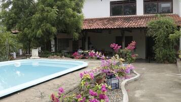 Piscina cercada por um jardim com flores cor-de-rosa e um edifício com telhado ladrilhado.
