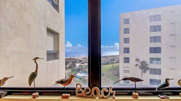 Janela com figuras de pássaros decorativas e vista para uma praia e edifícios.
