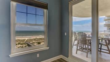 Quarto com uma grande janela com vista para a praia e varanda com mobiliário externo.