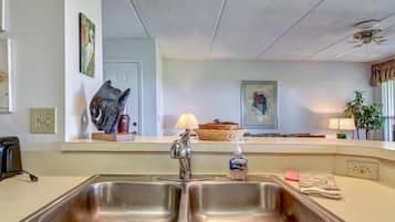 Cozinha com pia de aço inoxidável dupla, geladeira e micro-ondas. Há uma escultura decorativa de peixe no balcão e um quadro na parede.