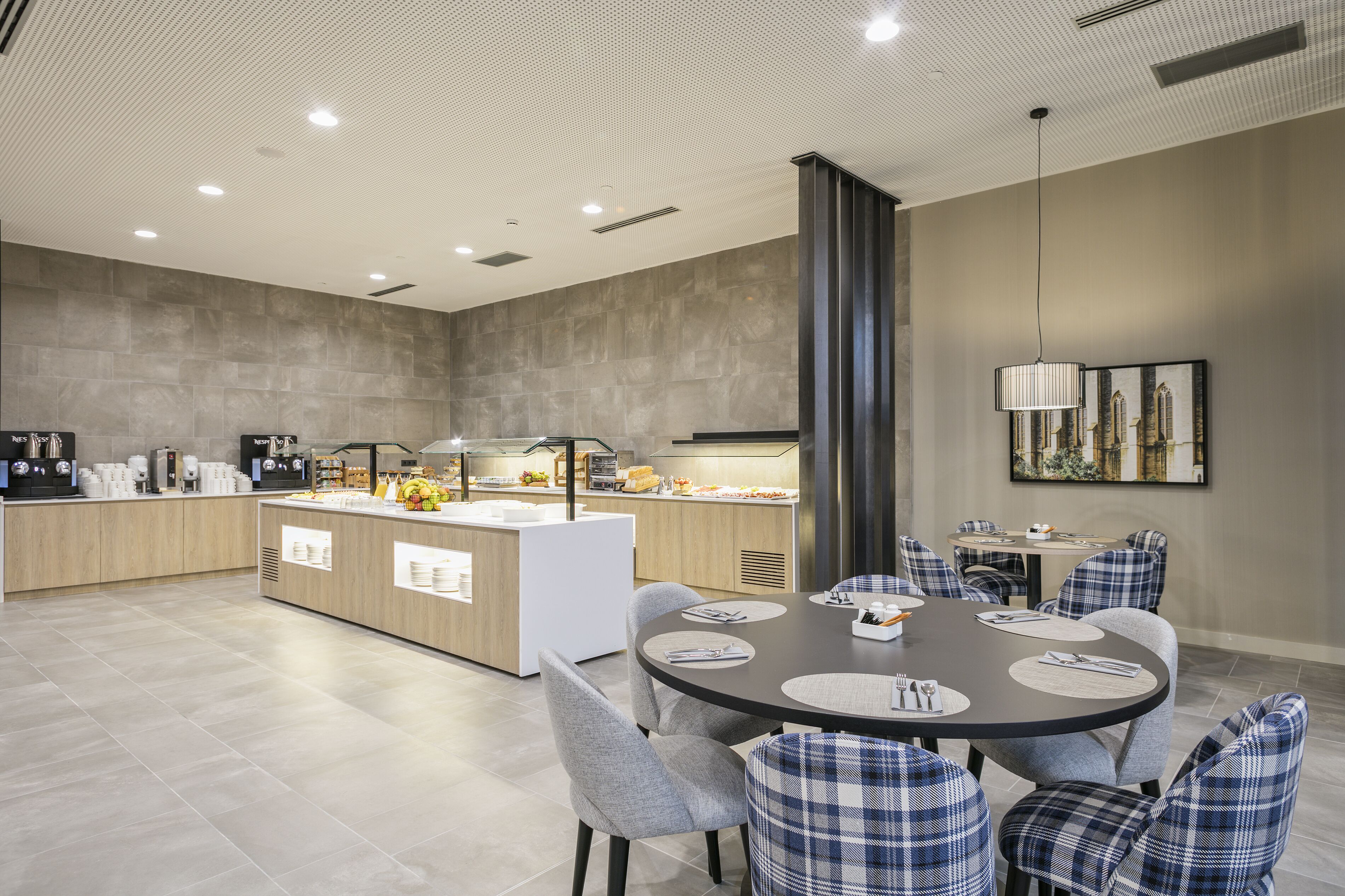 Uma cozinha moderna com uma ilha central, uma área de refeições com uma mesa redonda e cadeiras xadrez, e um quadro grande na parede.
