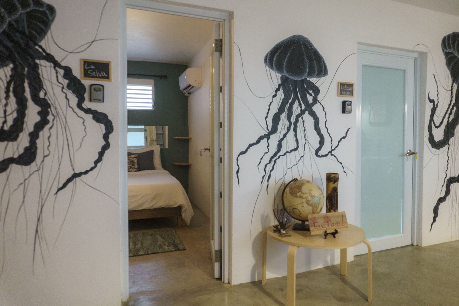 Quarto com uma cama, uma mesinha com um globo e uma placa, e paredes decoradas com arte abstrata em preto.