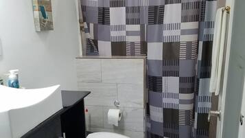 Casa de banho com sanita branca, armário preto, cortina de chuveiro com padrão geométrico e porta-toalhas fixado na parede.