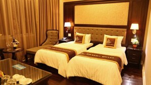 Quarto de hotel com duas camas, área de estar e mesa com copos e pratos.