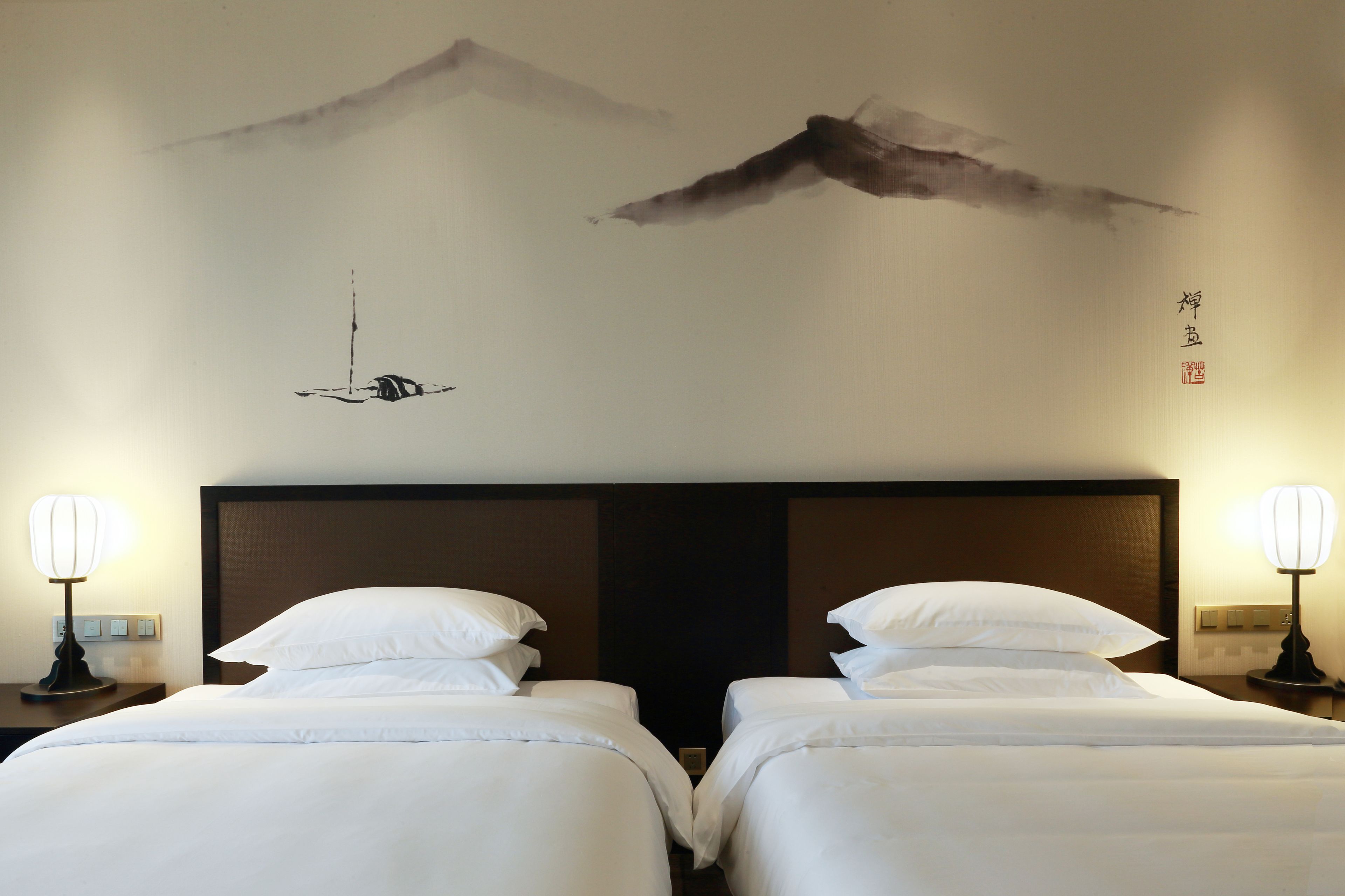 Quarto de hotel com duas camas, cabeceira de madeira e parede com pintura de montanhas e um veleiro.