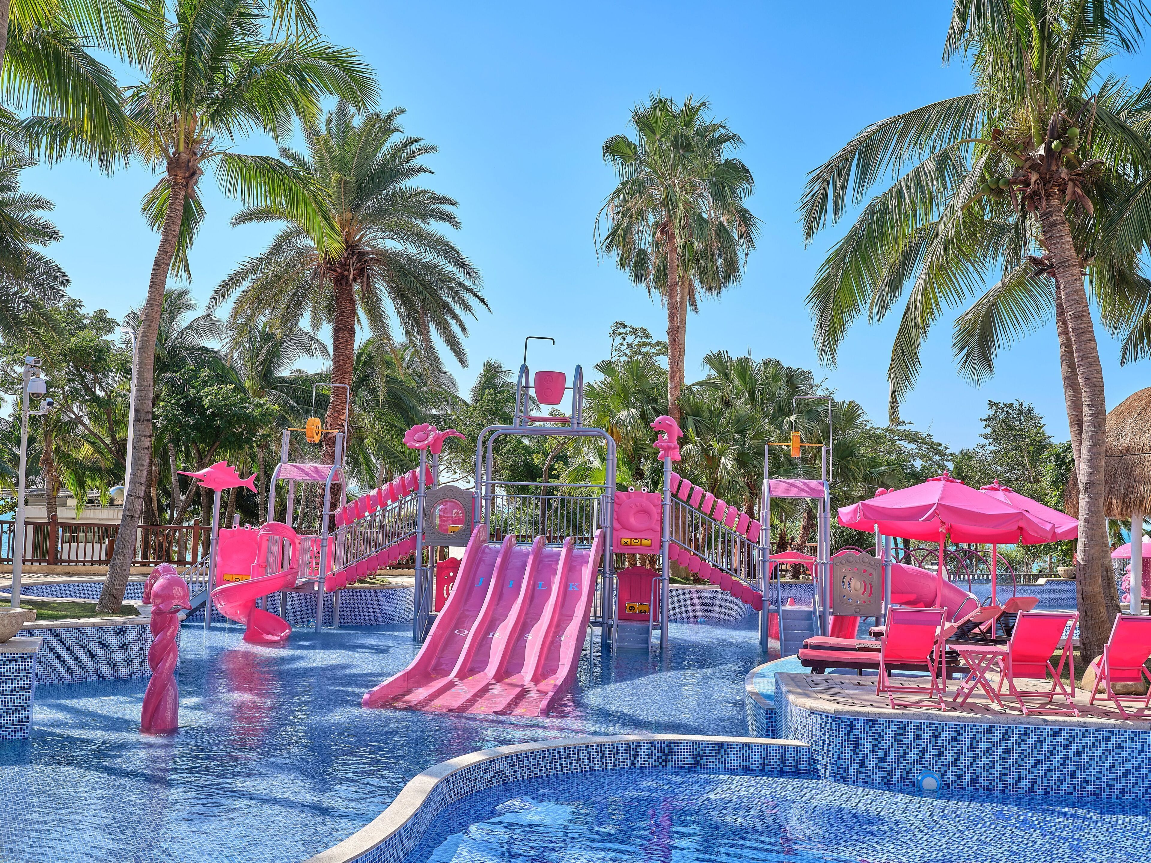 Uma área de piscina com toboáguas e guarda-sóis cor-de-rosa.