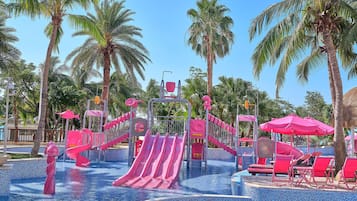 Uma área de piscina com toboáguas e guarda-sóis cor-de-rosa.