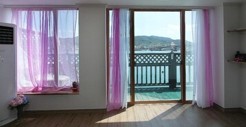 Quarto com uma grande porta de vidro deslizante que dá para uma varanda com vista para um corpo d'água e colinas.