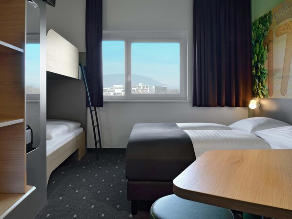 Quarto de hotel com beliche, escrivaninha e vista para prédios pela janela.