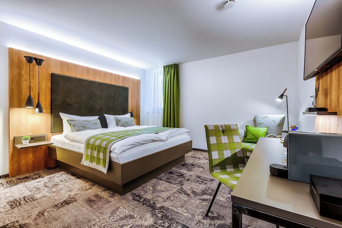 Quarto de hotel moderno com uma cama grande, uma escrivaninha com computador e uma televisão.