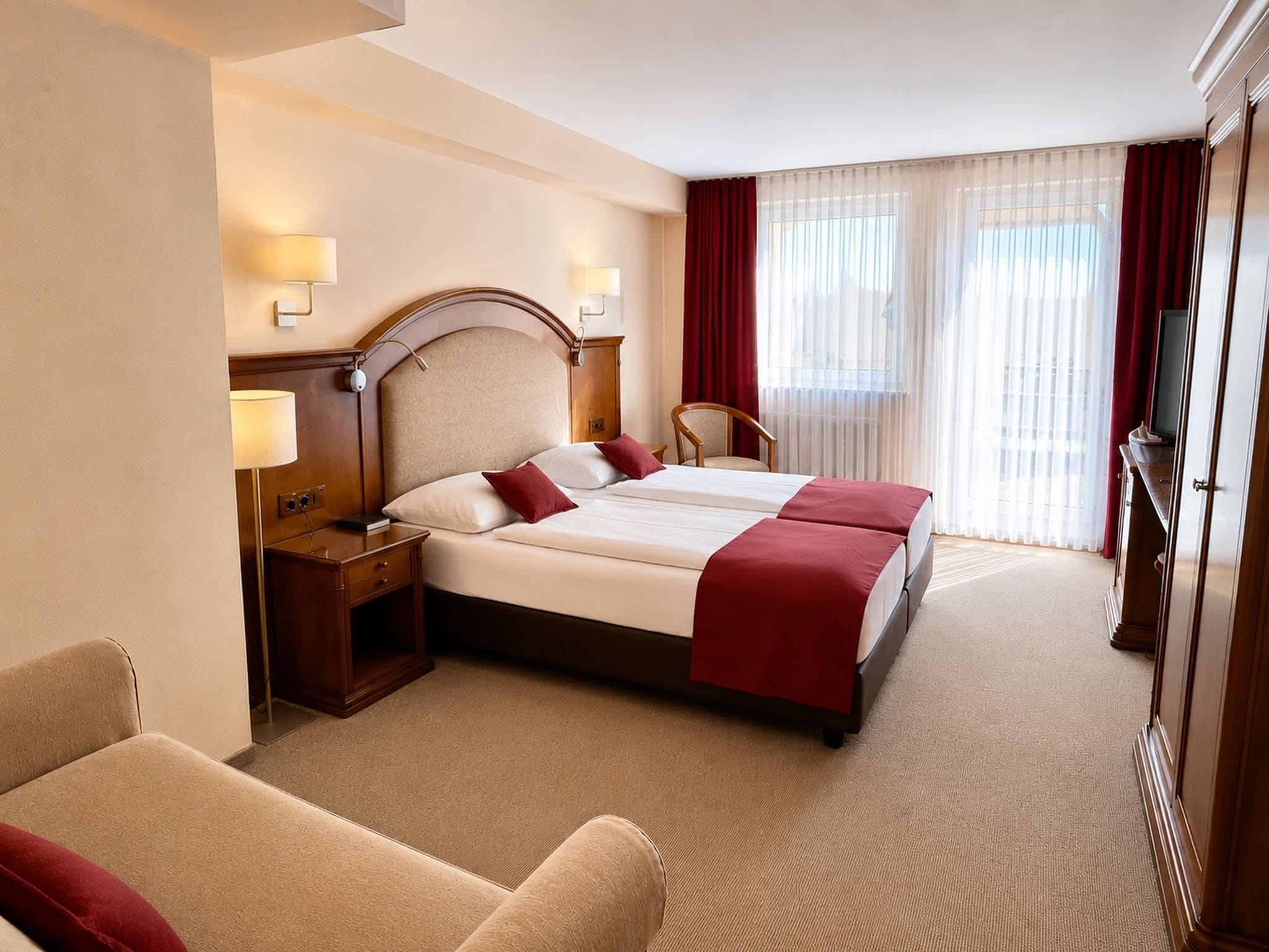Quarto de hotel com uma cama grande, duas mesas de cabeceira, uma cadeira, televisão e janela com cortinas.