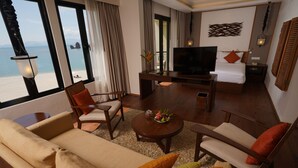 Quarto de hotel com sofá, poltronas, televisão, cama e vista para o mar.