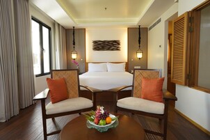 Quarto de hotel com cama, duas cadeiras, uma mesa com frutas e uma janela com cortinas.