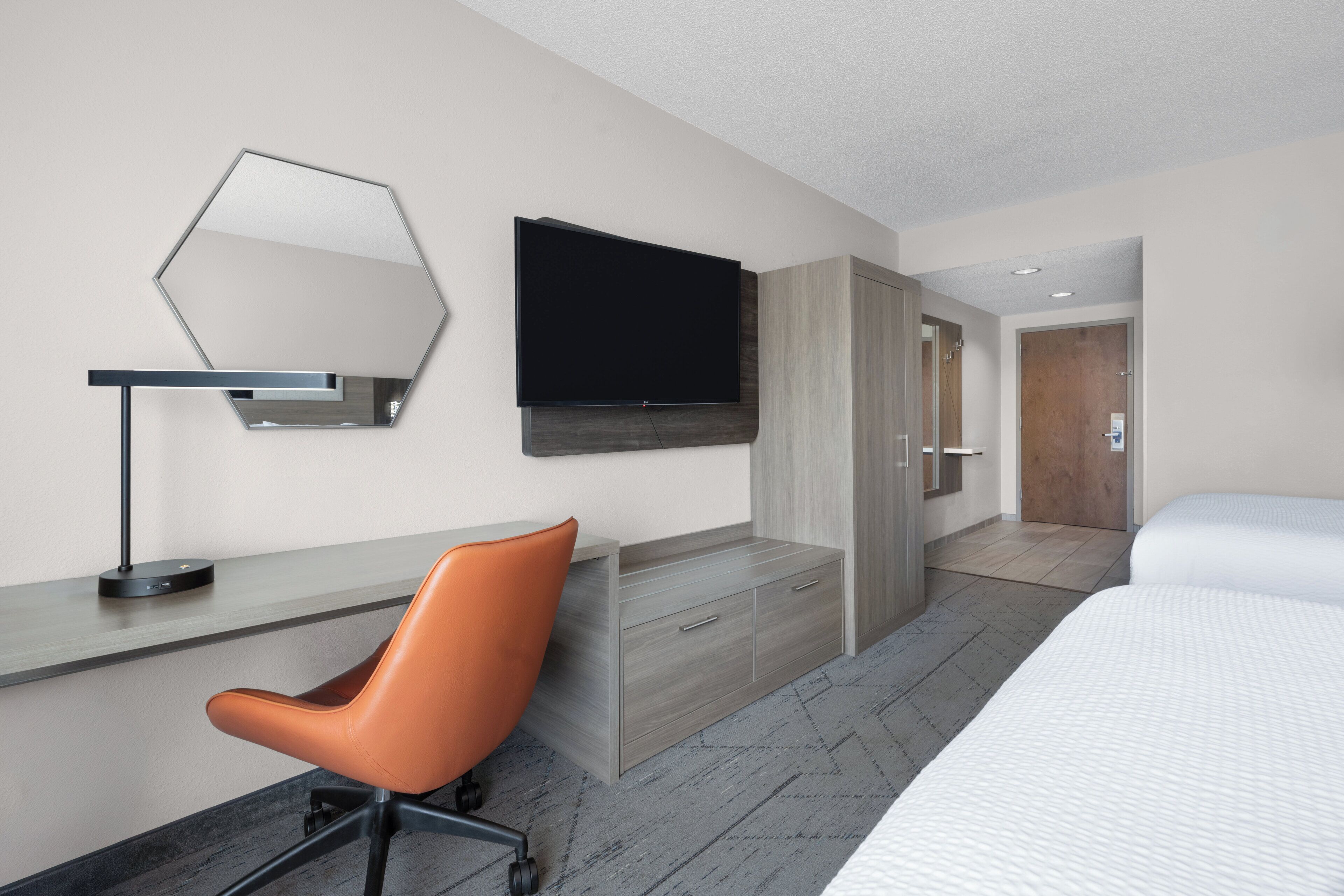Quarto de hotel com cama, escrivaninha com cadeira, televisão na parede e guarda-roupa.