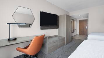 Quarto de hotel com cama, escrivaninha com cadeira, televisão na parede e guarda-roupa.