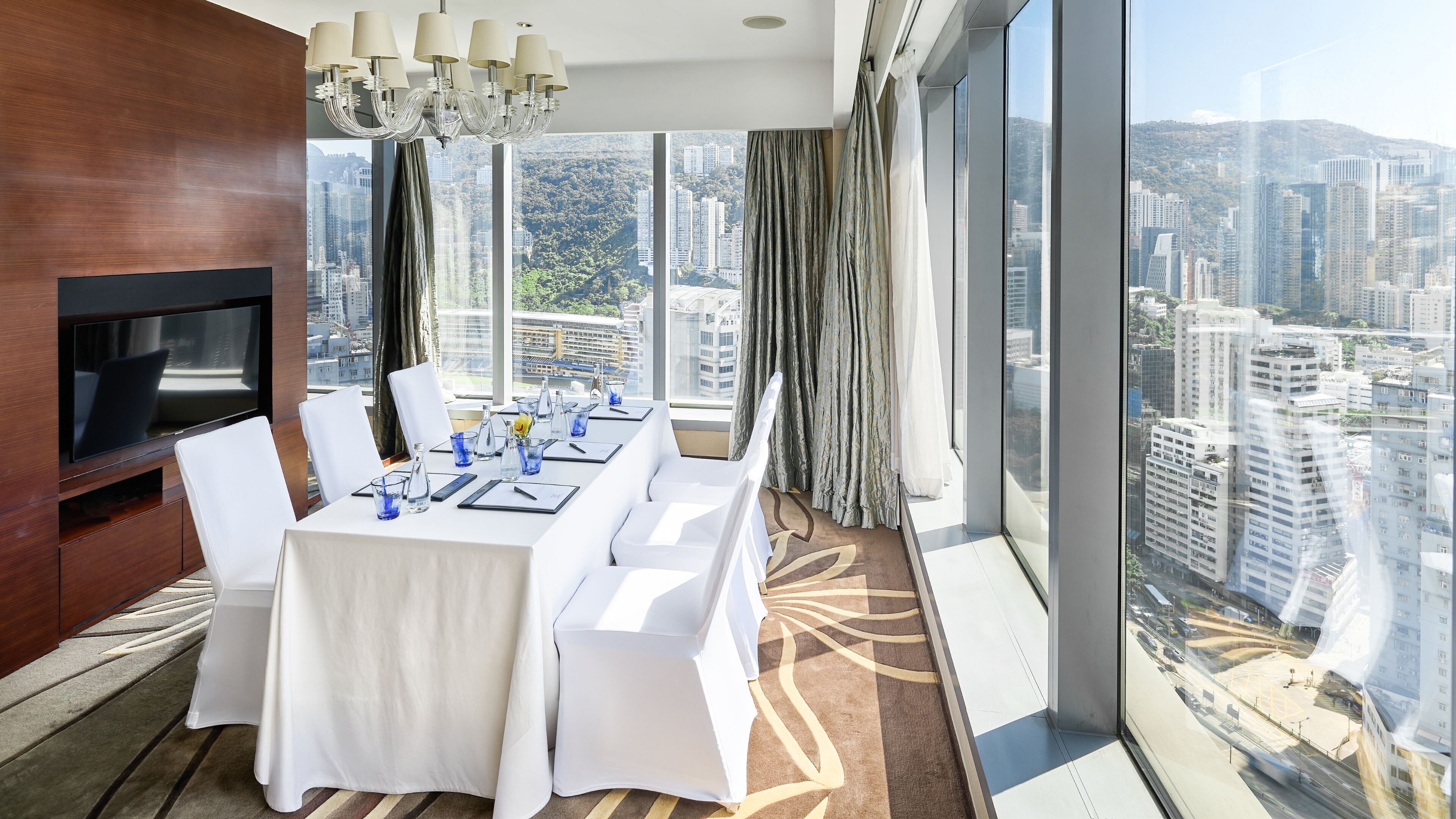 Quarto de hotel com uma grande mesa de jantar, televisão e vista para a cidade.