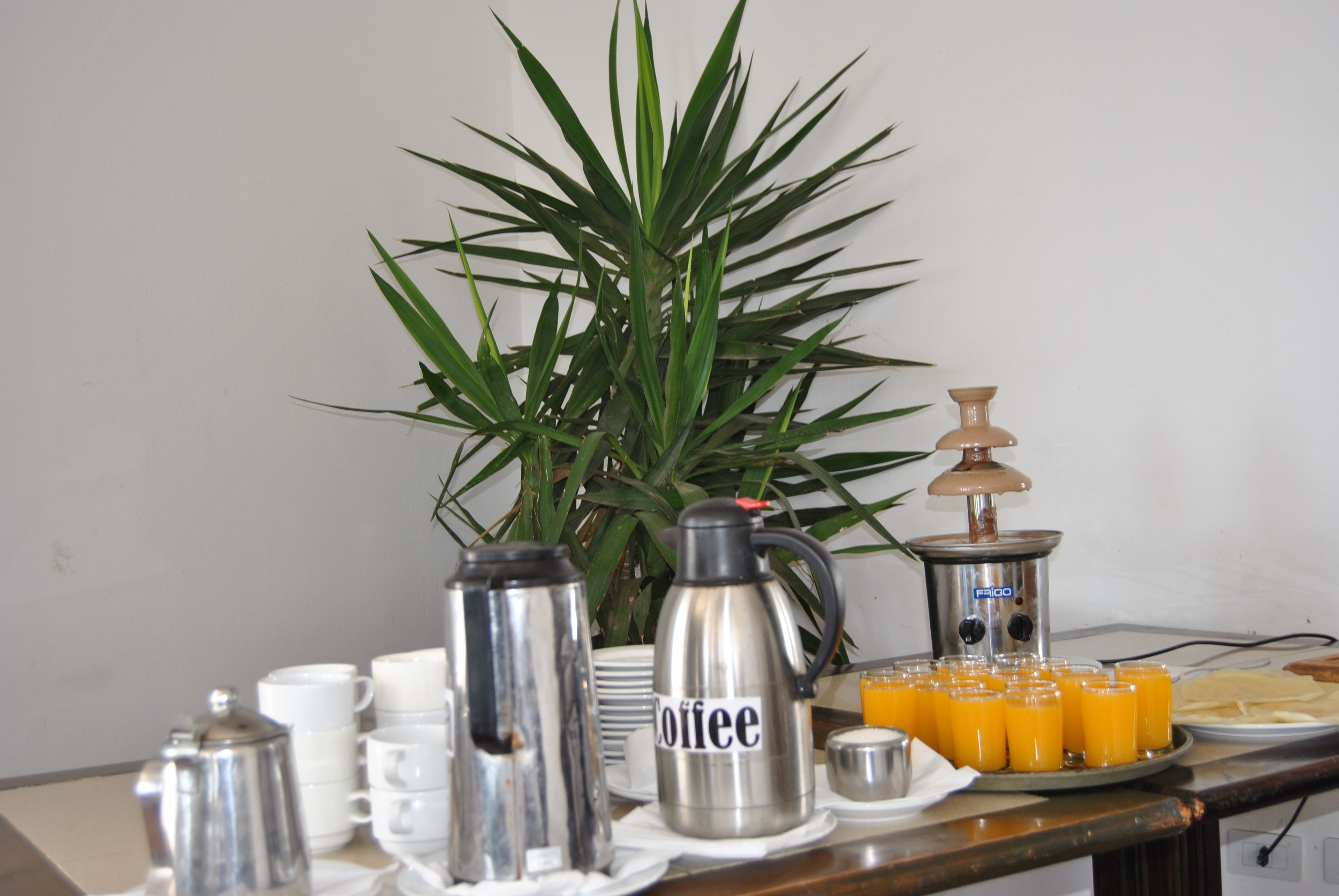 Disposição de buffet de café da manhã com cafeteiras, xícaras e suco de laranja.