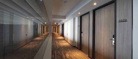 Corredor de hotel com piso de carpete, portas de madeira e uma placa de número em uma das portas.