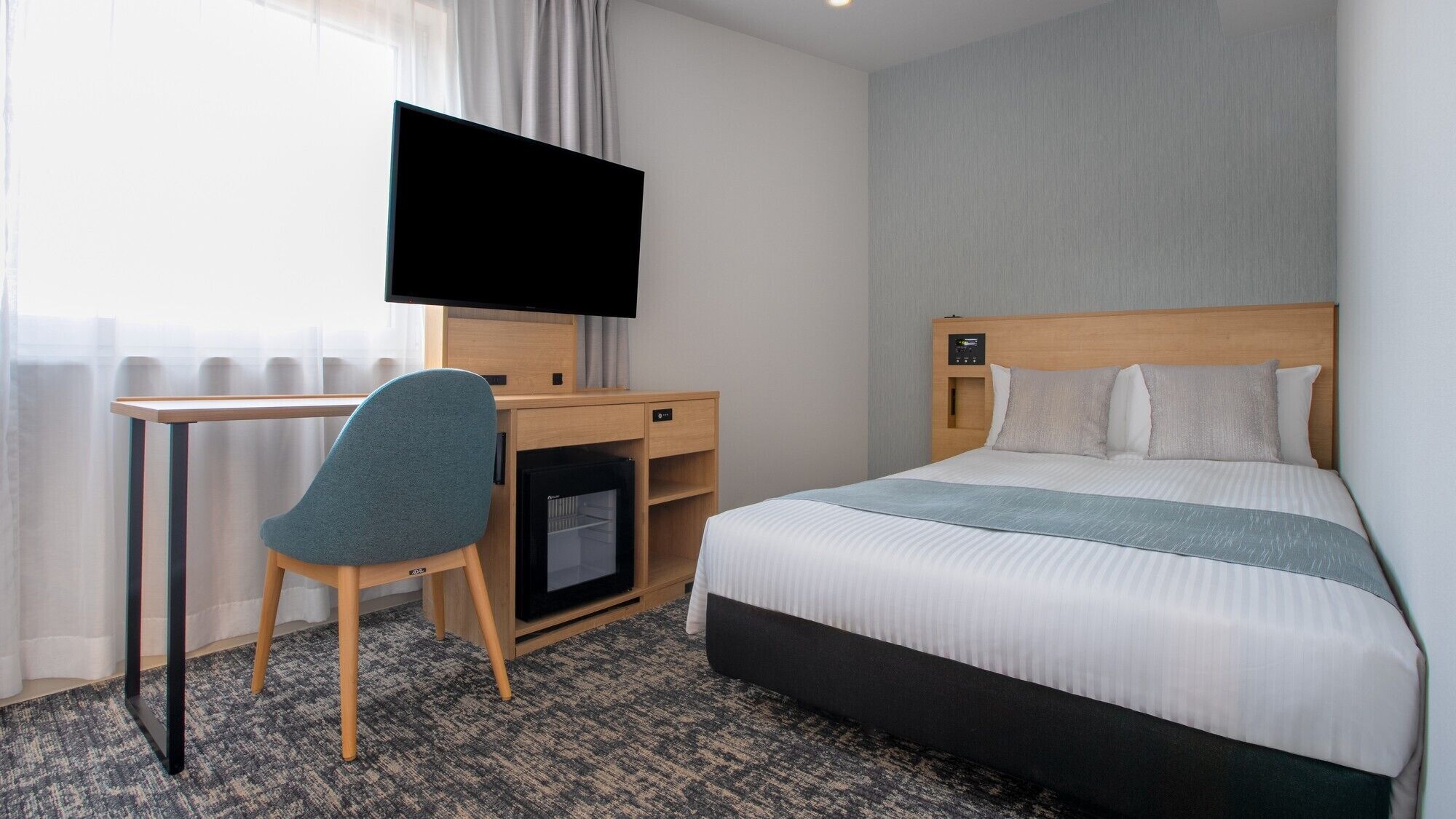 Quarto de hotel com cama, secretária, cadeira, televisão e um pequeno aquecedor.