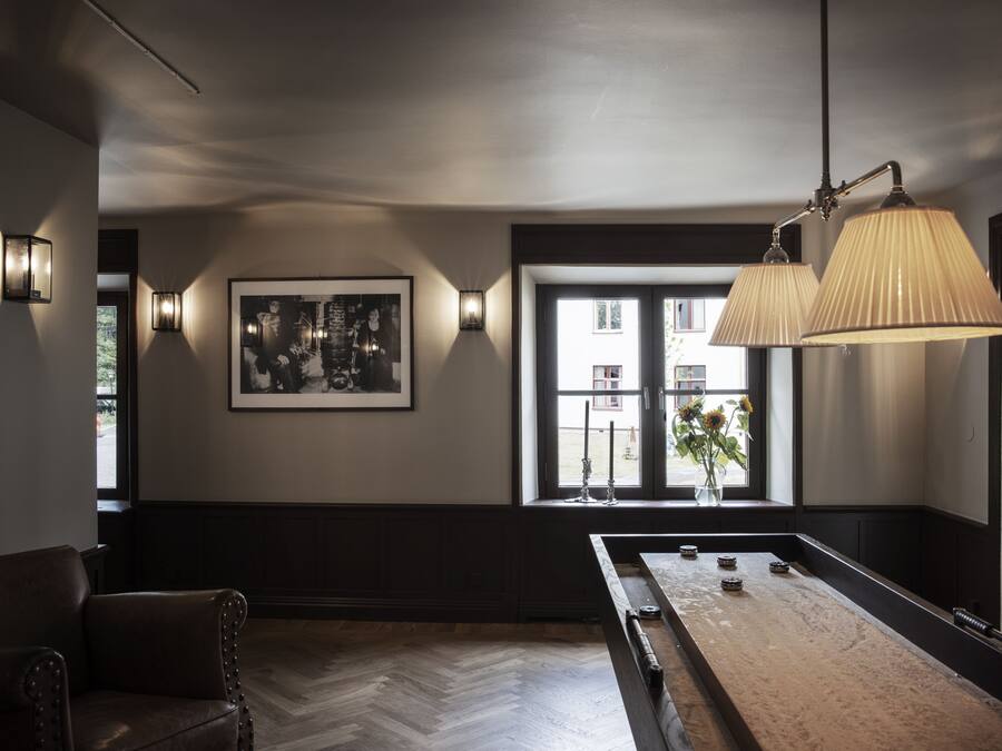 Um ambiente com pouca luz, com uma mesa de bilhar, um quadro na parede e uma janela com vista para o exterior.
