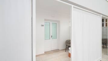 Quarto com porta de correr para uma varanda, uma cadeira e uma lixeira.