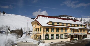 Um hotel tradicional europeu com telhado coberto de neve, várias janelas e uma placa indicando que é um restaurante e café.