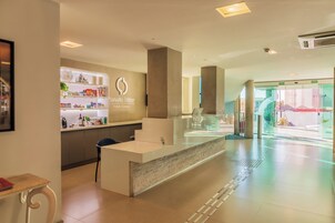 Uma área de recepção de hotel com balcão, espaço de espera e entrada por porta de vidro.