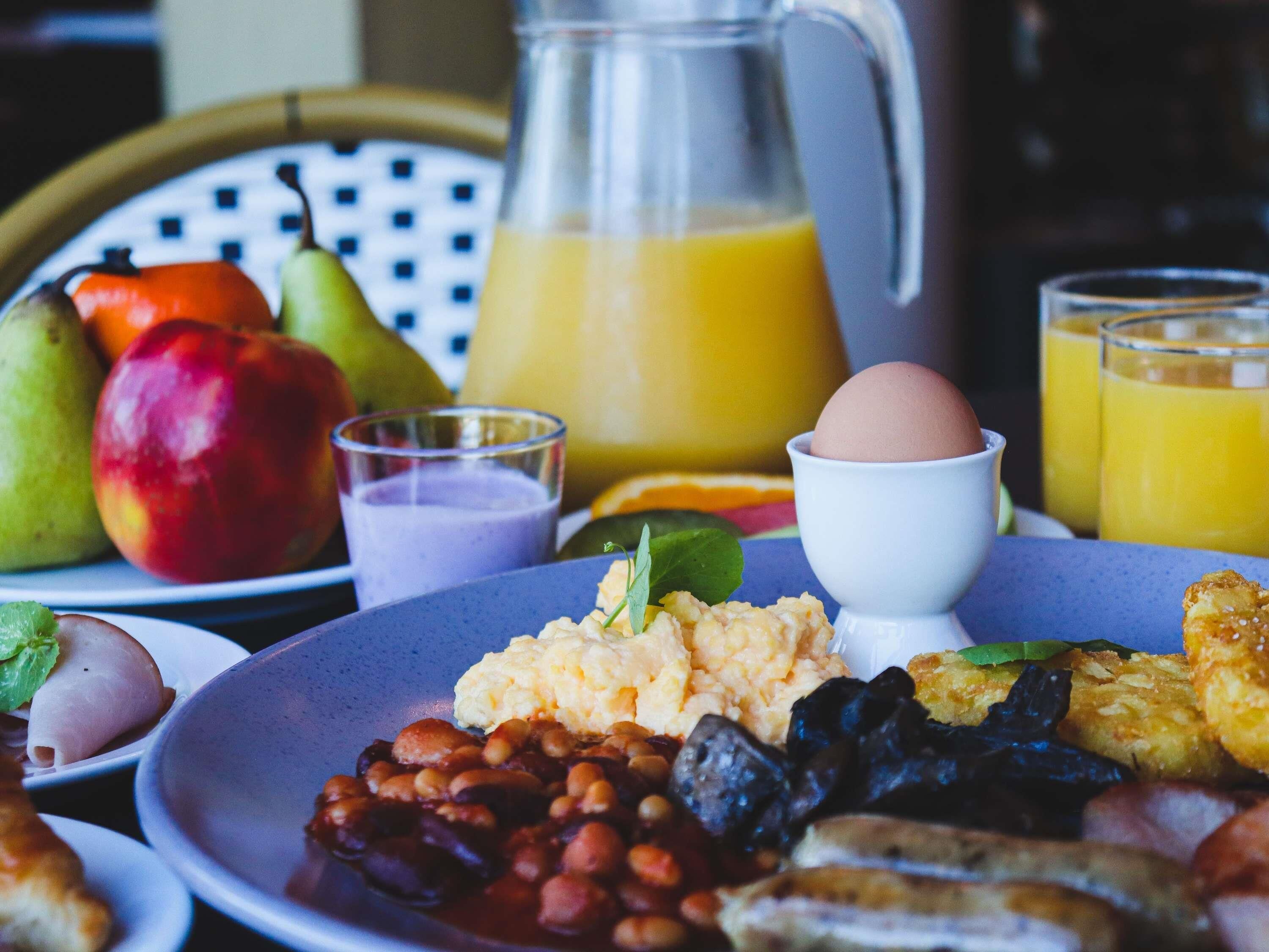 Disposição de café da manhã com ovos, torradas, feijão e frutas.