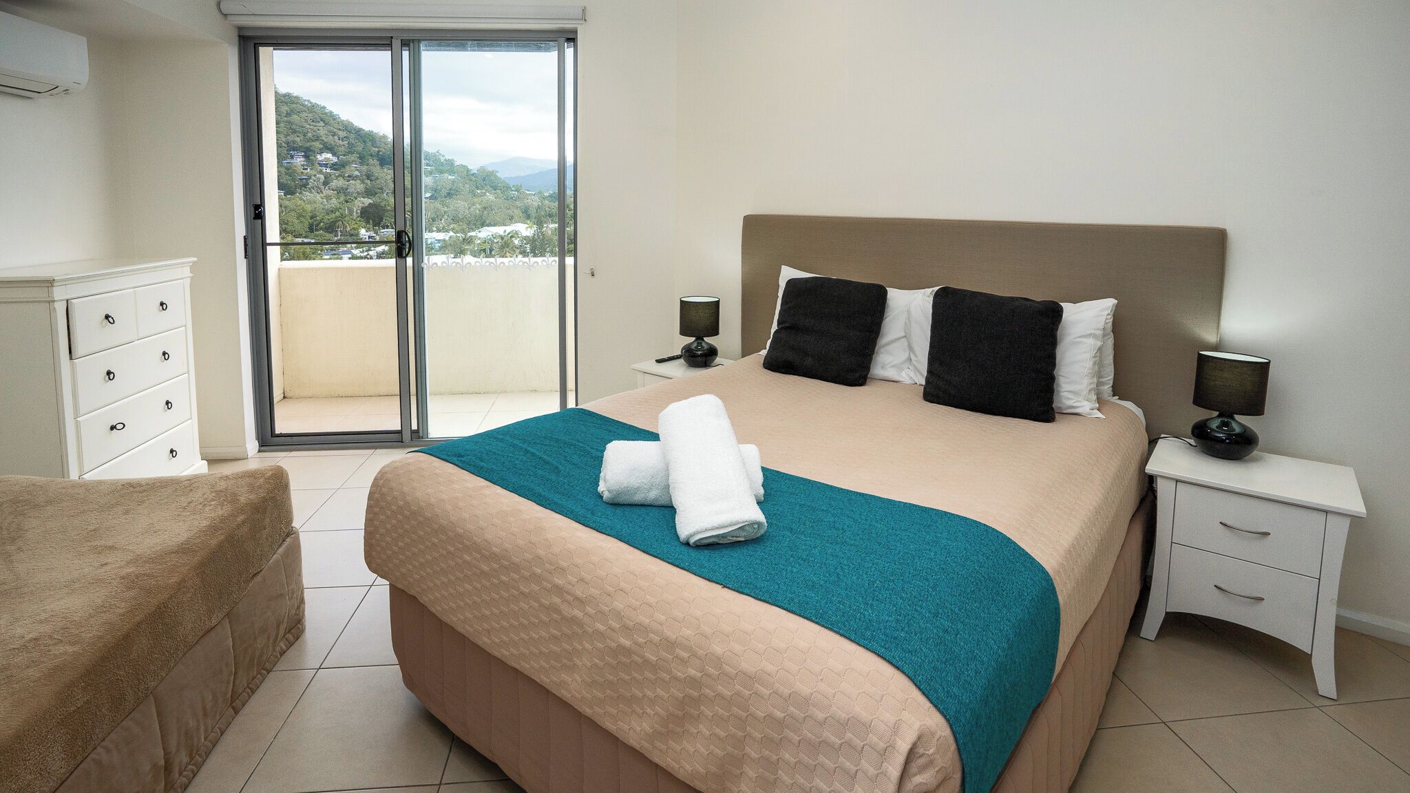 Quarto de hotel com uma cama, uma mesa de cabeceira, uma cadeira e uma porta de vidro corrediça para uma varanda.