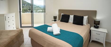 Quarto de hotel com uma cama, uma mesa de cabeceira, uma cadeira e uma porta de vidro corrediça para uma varanda.
