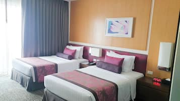 Quarto de hotel com duas camas, uma cabeceira de madeira, um quadro, uma mesinha de cabeceira e um relógio.