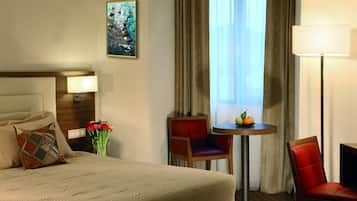 Quarto de hotel com cama, escrivaninha, cadeira, abajur, quadro na parede e janela com cortinas.