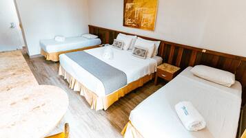 Quarto de hotel com três camas, uma cabeceira de madeira, uma pequena mesa de cabeceira e uma obra de arte na parede.