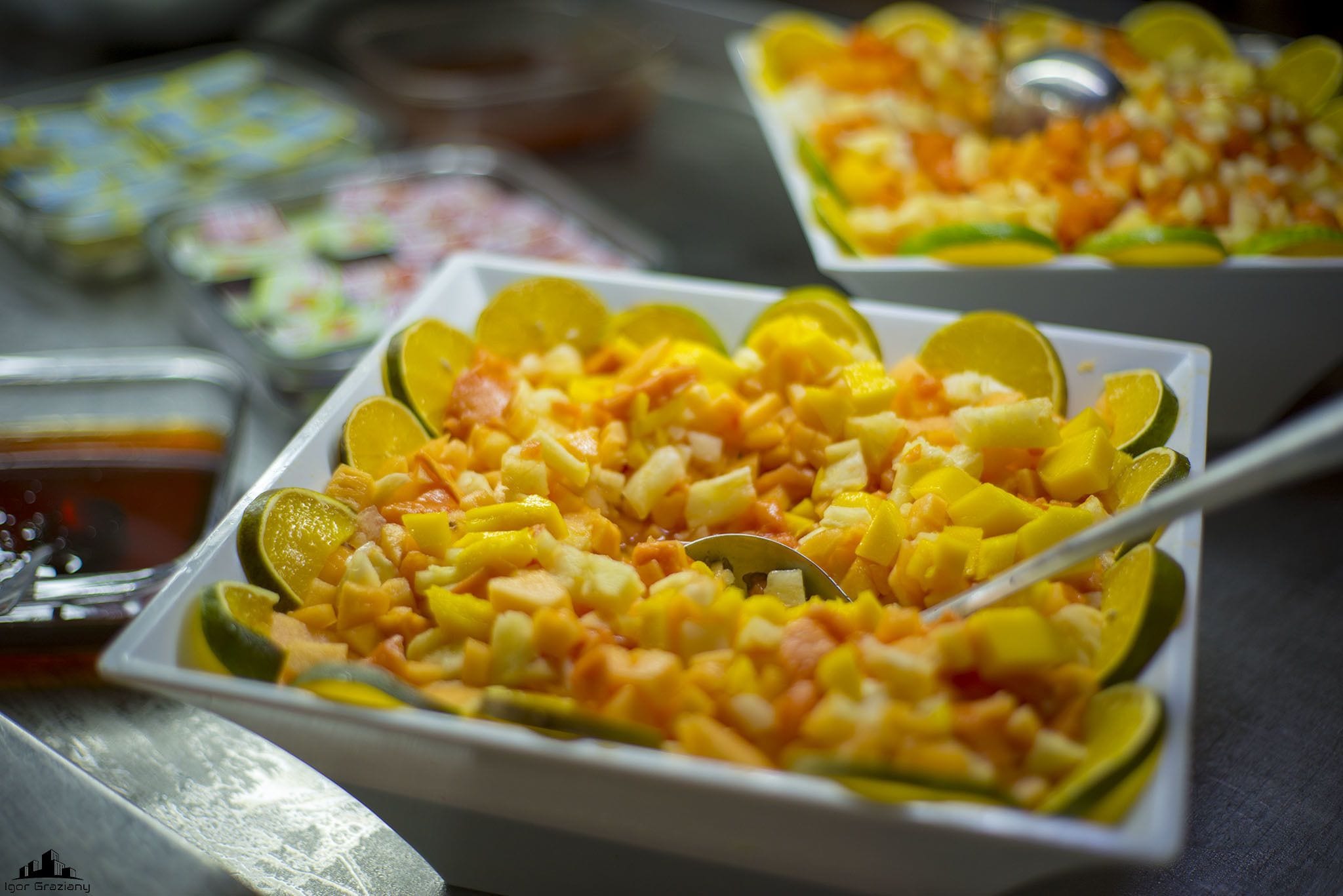 Buffet com diversos pratos, incluindo salada de frutas com manga e limão picados.