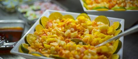 Buffet com diversos pratos, incluindo salada de frutas com manga e limão picados.